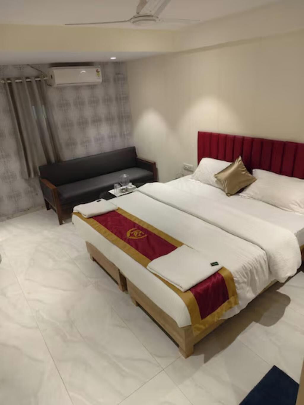 Quarto de hotel com cama, sofá, ar condicionado e cortina.