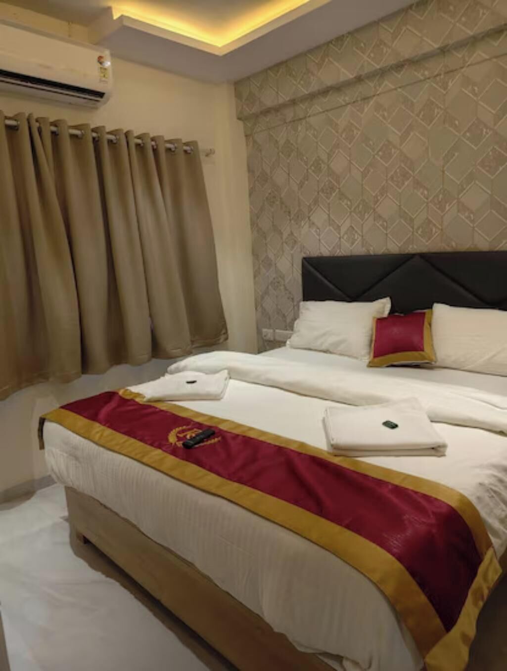 Quarto de hotel com cama, cortinas, aparelho de ar condicionado e parede estampada.