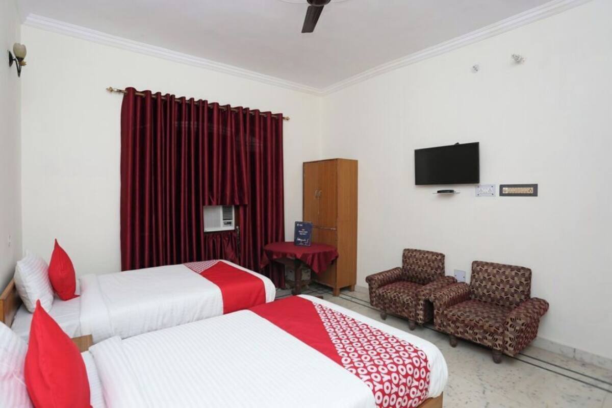 Quarto de hotel com duas camas, televisão, guarda-roupa, mesa pequena e um sofá estampado.