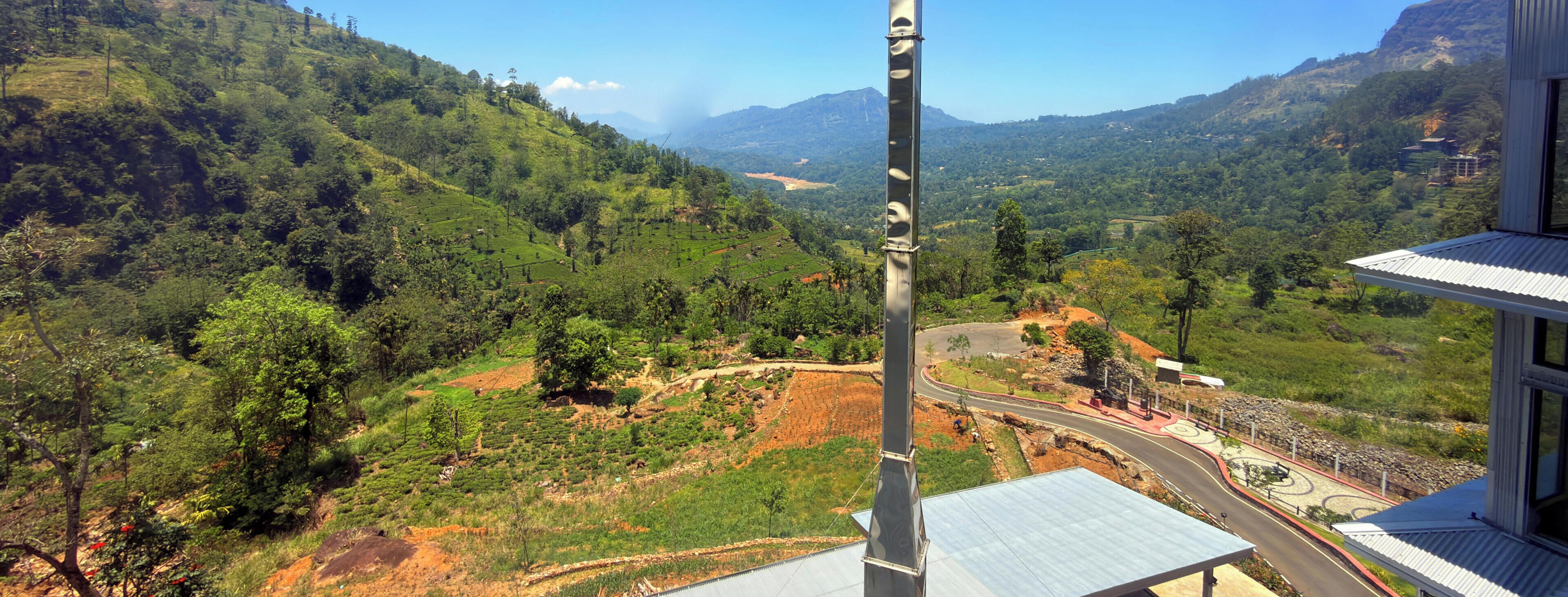 Vista de um vale verdejante com campos em socalcos, uma estrada sinuosa e um edifício com telhado de metal.