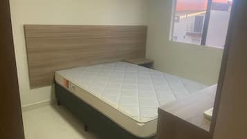 Um quarto com cama, cabeceira de madeira, uma mesinha de cabeceira e uma janela.