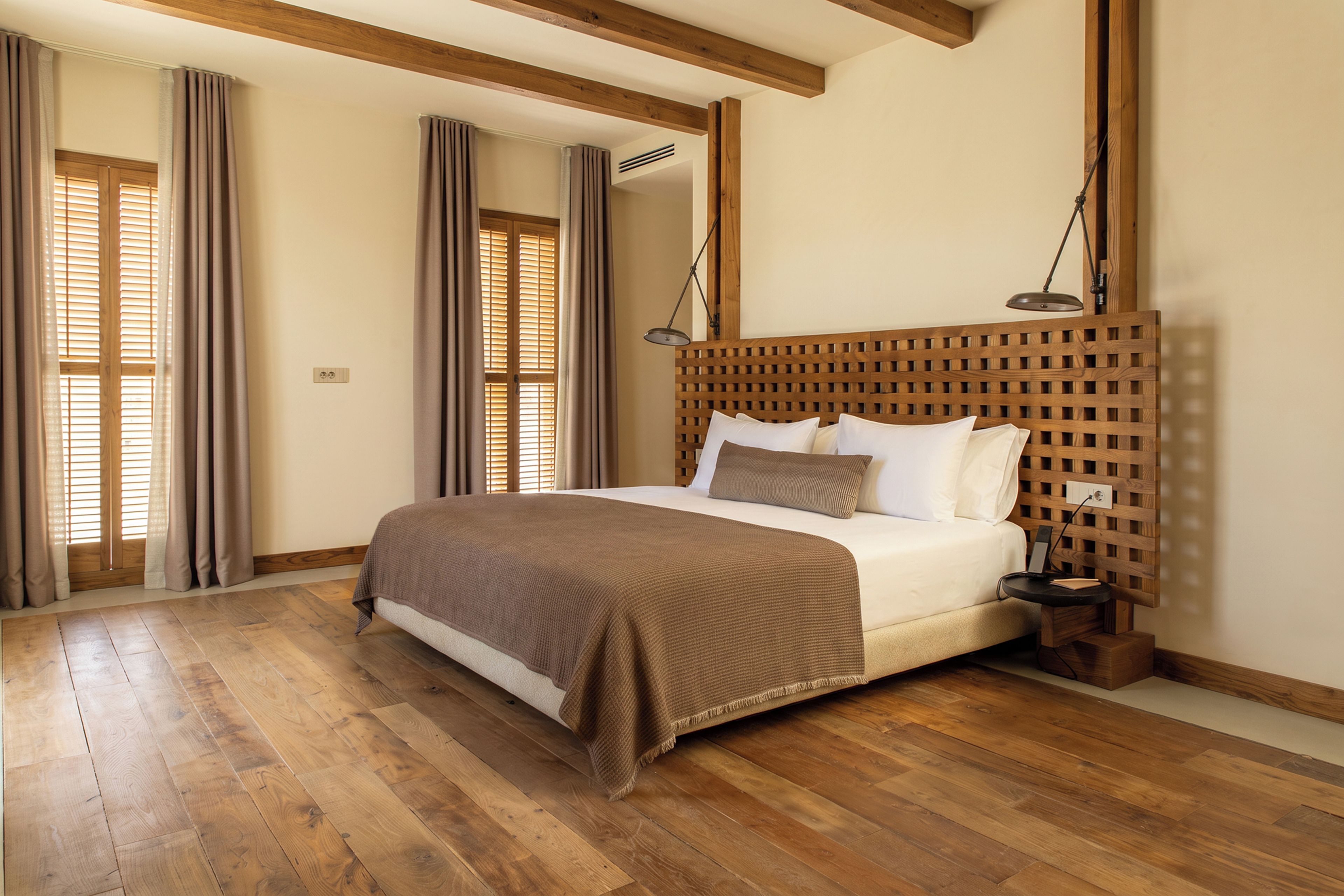 Quarto com estrutura de cama de madeira, mesa de cabeceira com abajur e janela com cortinas.