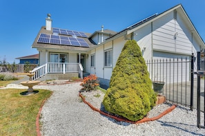 Uma casa com painéis solares, gramado bem cuidado, uma grande árvore conífera e uma entrada com portão.