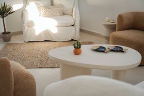 Uma sala de estar moderna com um sofá branco, uma mesa de centro redonda e um vaso de planta.