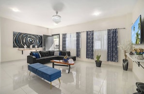 Uma sala de estar moderna com um sofá de couro preto, um banco azul, uma mesa de centro e um candelabro.