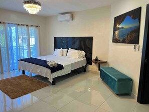 Quarto com cama grande, um banco, um quadro e um candelabro.