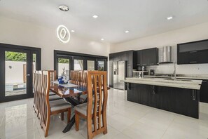 Uma cozinha moderna com armários escuros, uma ilha central e um espaço de refeições com mesa de vidro e cadeiras de madeira.