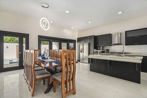 Uma cozinha moderna com armários escuros, uma ilha central e um espaço de refeições com mesa de vidro e cadeiras de madeira.