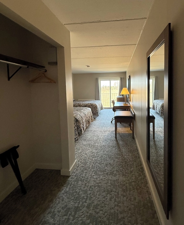 Quarto de hotel com cama, escrivaninha, cadeira, abajur, espelho e cabideiro.