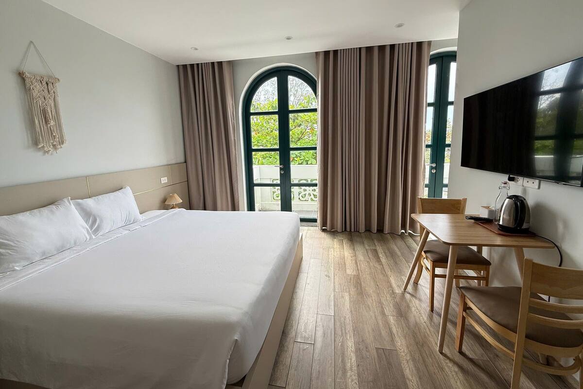 Quarto de hotel com cama, televisão, mesa e cadeiras, e janela com cortinas.