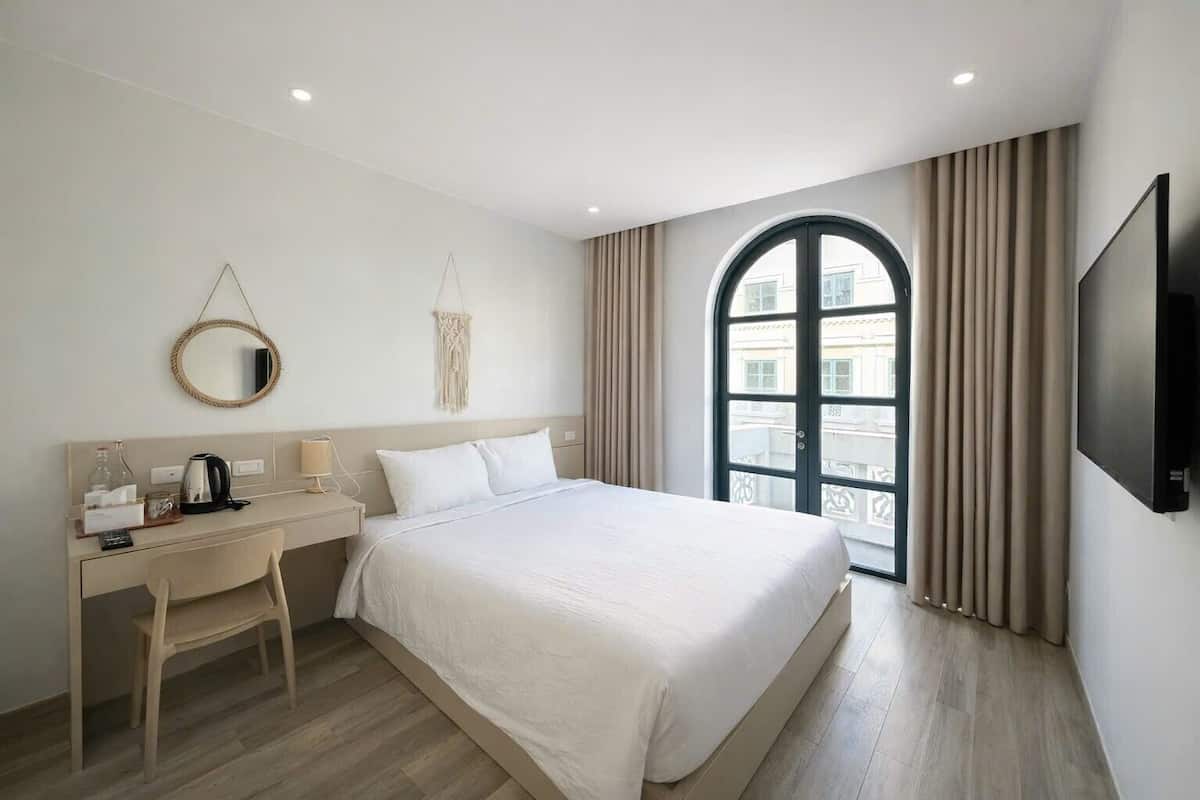Quarto de hotel com cama, escrivaninha, cadeira e televisão.