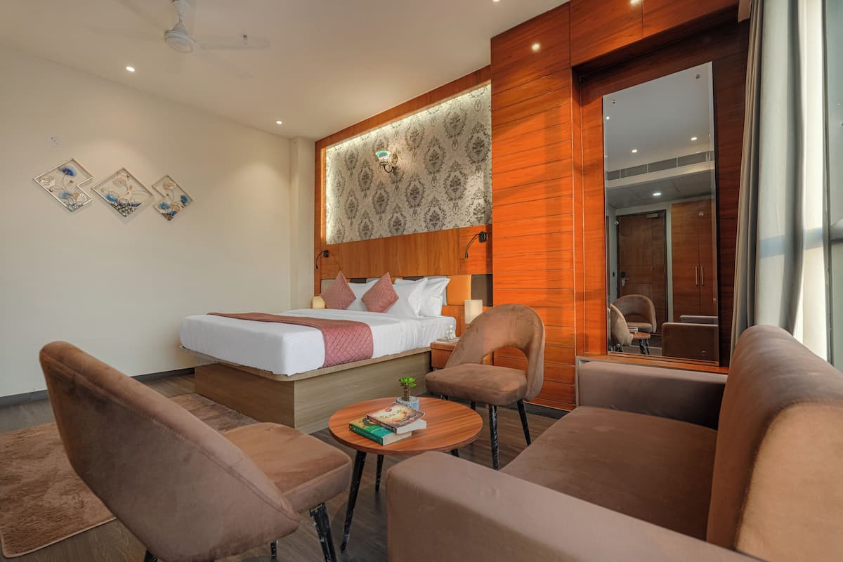 Quarto de hotel com cama, duas poltronas, uma mesinha, espelho e uma parede com painéis decorativos.