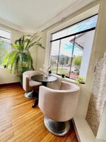 Quarto moderno com uma mesa redonda, duas cadeiras, um vaso de planta e uma grande janela com vista.