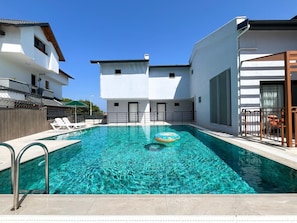 Piscina retangular com água cristalina, rodeada por edifícios modernos e uma área de estar com cadeiras.