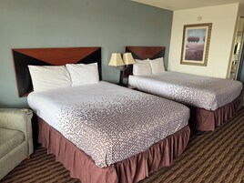 Quarto de hotel com duas camas, uma mesinha de cabeceira, uma luminária e um quadro na parede.