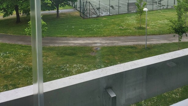 Vista de um parque com quadra de basquete, árvores e uma estrada.
