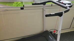 Uma bicicleta ergométrica com visor digital, uma esteira e uma janela com vista para árvores.