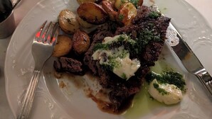 Um prato com bife, batatas assadas e um molho cremoso, acompanhado de garfo e faca.