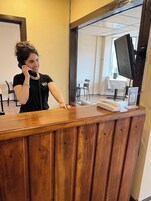 Uma mesa de recepção com acabamento em madeira, um telefone e uma televisão fixada na parede.