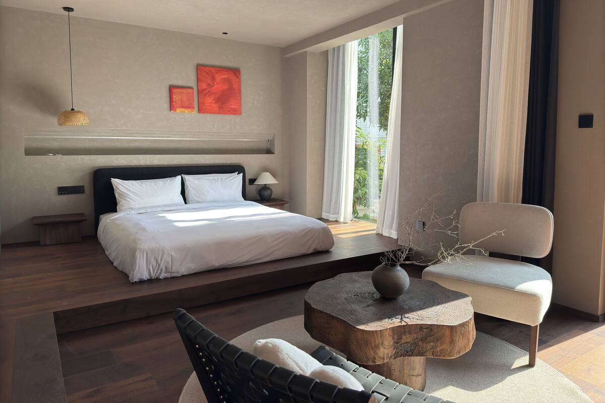 Quarto moderno com uma cama grande, mesas de cabeceira, uma mesa de centro redonda, uma cadeira e vista para o verde lá fora.