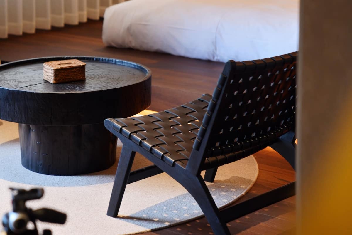 Quarto de hotel com uma cama, uma luminária, uma mesa de centro redonda e uma cadeira.