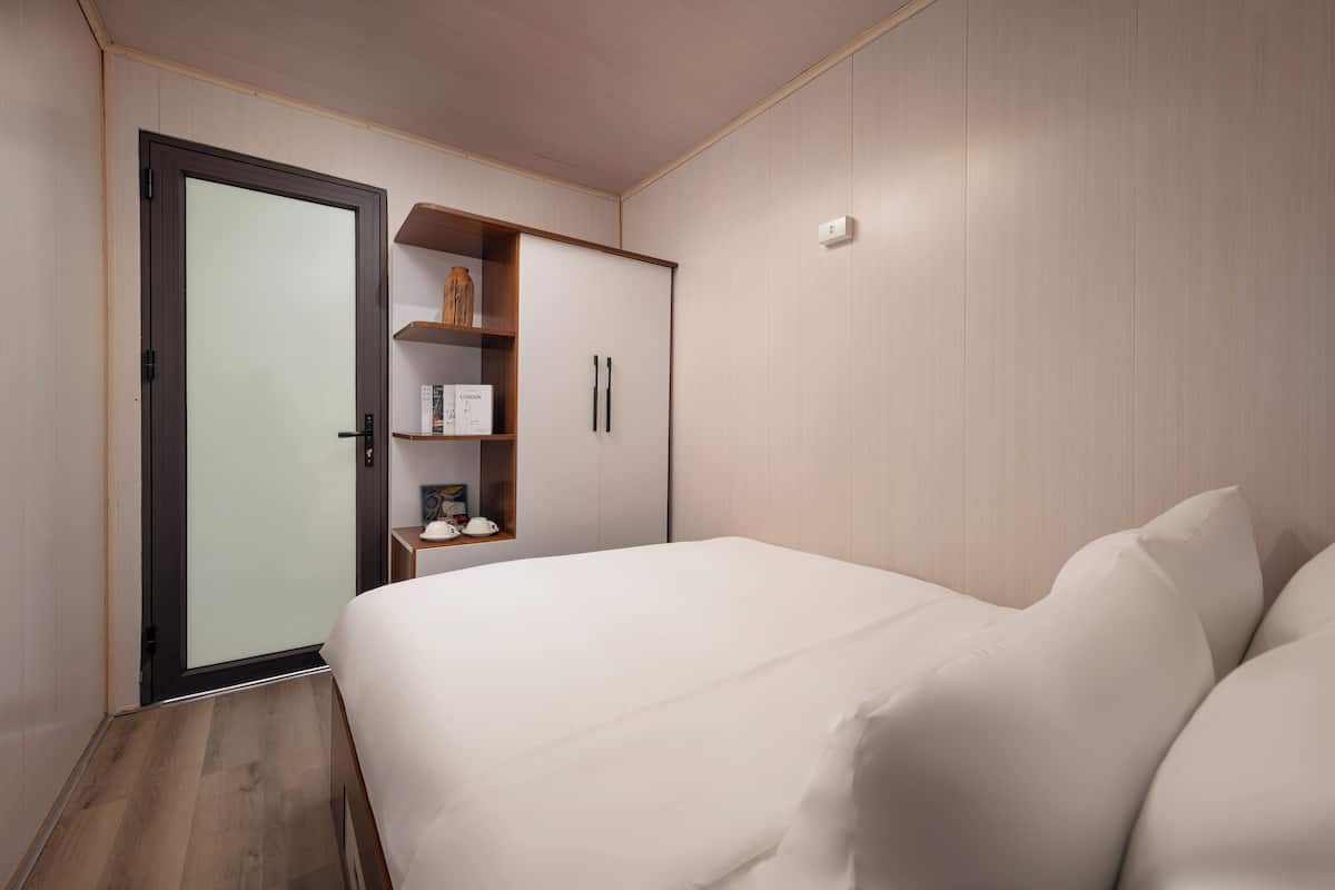 Quarto com cama, guarda-roupa, prateleira com objetos e porta.