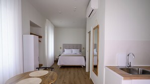 Quarto de hotel com cama, mesa de cabeceira e uma área de kitchenette.