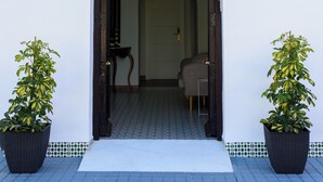 Uma porta que dá para um quarto com piso de azulejos, um lustre pendurado e duas plantas em vasos.