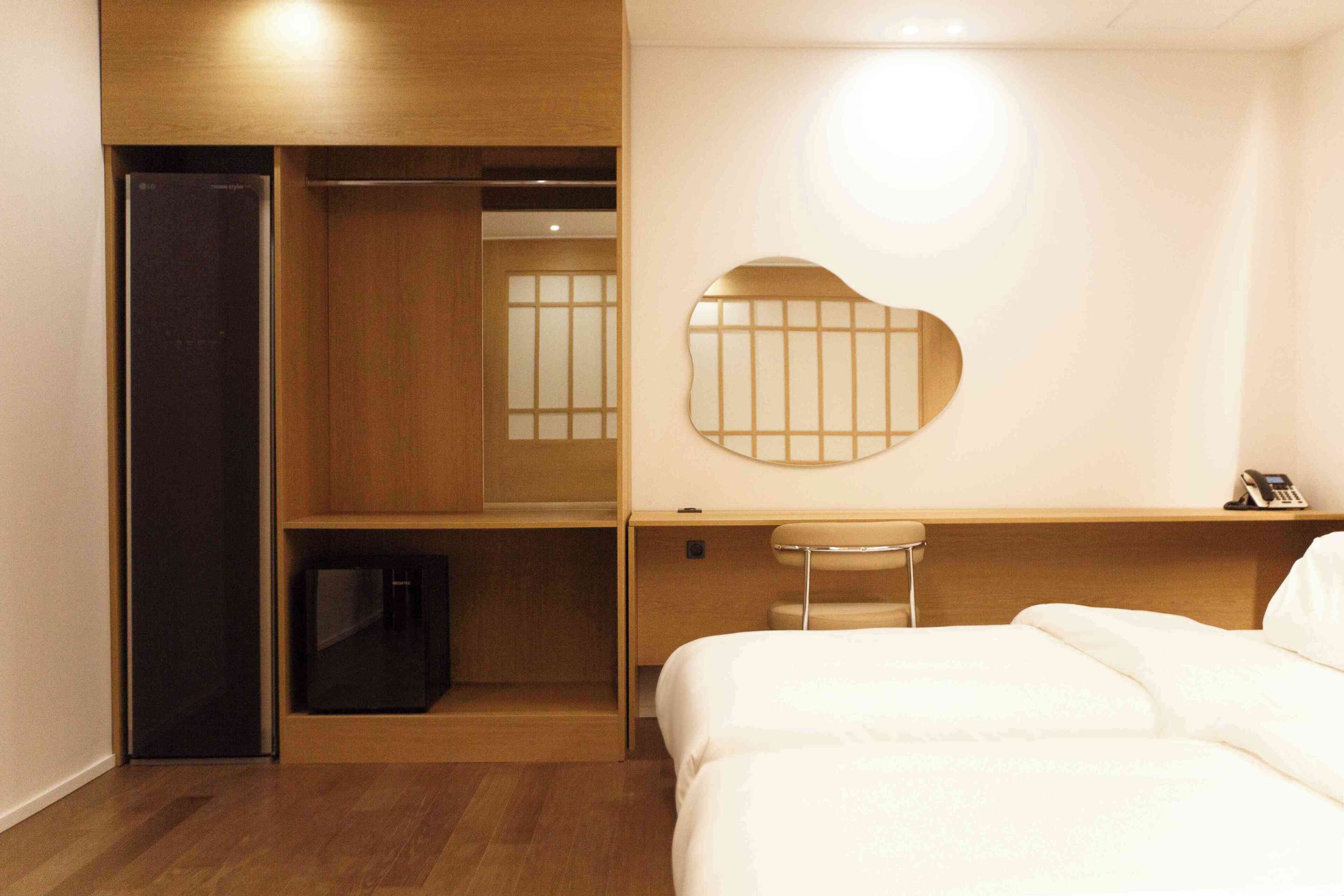 Quarto de hotel com uma cama, escrivaninha, cadeira, guarda-roupa e espelho.