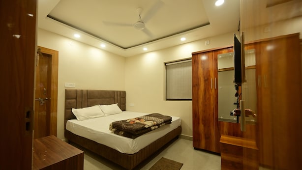 Quarto com cama, ventoinha no teto, iluminação embutida, guarda-roupa de madeira e uma mesinha.