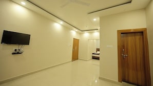 Quarto de hotel com televisão de tela plana na parede, ventoinha no teto e porta de madeira.