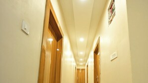 Corredor de hotel com portas de madeira, chão de azulejo e iluminação embutida.