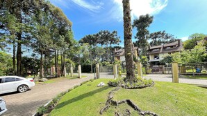 Uma área residencial com calçada pavimentada, um carro branco estacionado na lateral, e uma casa com telhado cerâmico ao fundo.