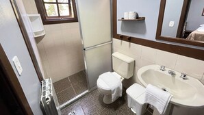 Casa de banho com chuveiro, sanita e lavatório, e um espelho.