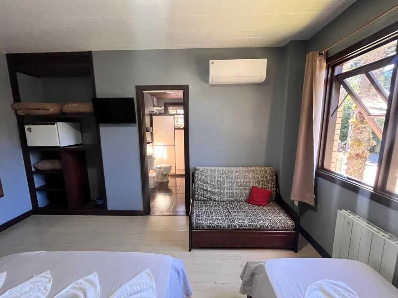 Quarto com duas camas, um sofá, um guarda-roupa e ar condicionado.