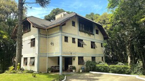Um edifício de vários andares com telhado de telhas, rodeado por vegetação e um caminho de acesso pavimentado.