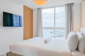 Quarto de hotel com cama, televisão, janela grande e luminária no teto.