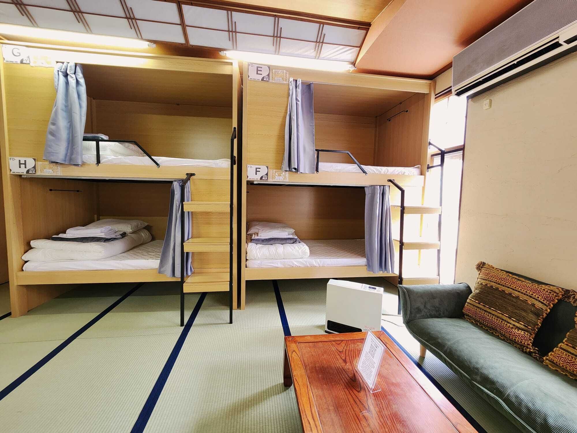 Quarto de dormitório com beliches, futon, piso de tatame e ventilador de teto.