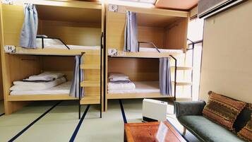 Quarto de dormitório com beliches, futon, piso de tatame e ventilador de teto.
