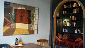 Uma sala de jantar com mesa, cadeiras, um quadro e uma estante de livros.