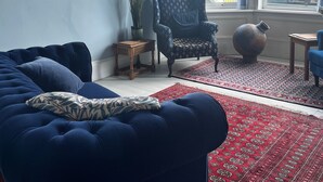 Uma sala de estar com um sofá azul, um tapete estampado, uma poltrona e um vaso grande.