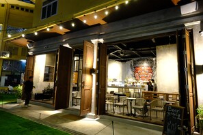 Uma área externa com mesas e cadeiras, um bar com garrafas e um mural na parede.
