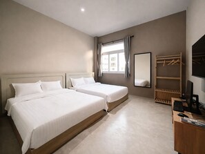 Quarto de hotel com duas camas, uma escrivaninha com computador, espelho e janela com cortinas.
