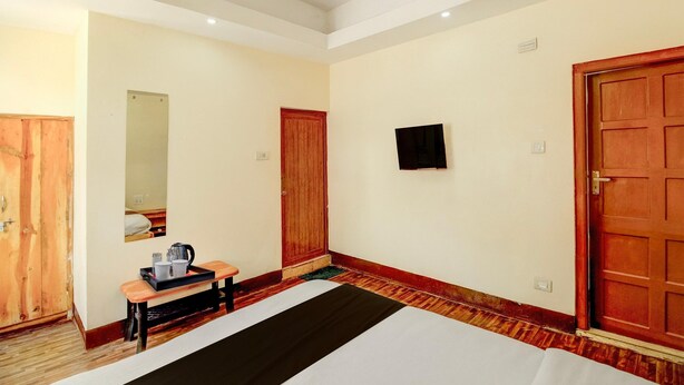 Quarto de hotel com uma cama, uma escrivaninha com chaleira, um espelho, uma televisão e uma porta de madeira.