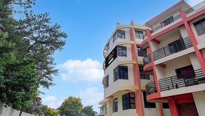 Um edifício residencial de vários andares, com varandas, entrada com portão e céu claro.