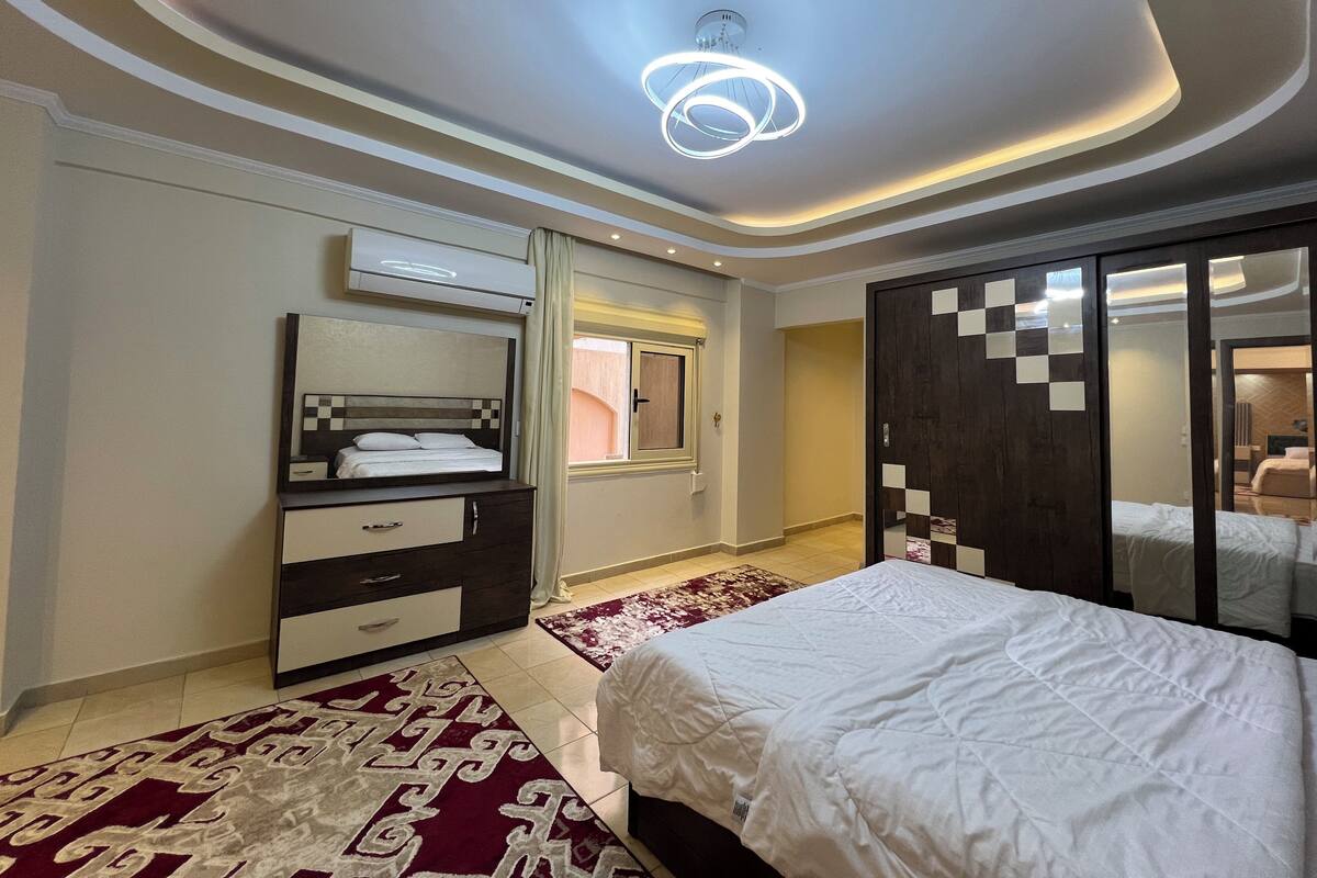 Quarto moderno com cama, cômoda, guarda-roupa e luminária de teto.