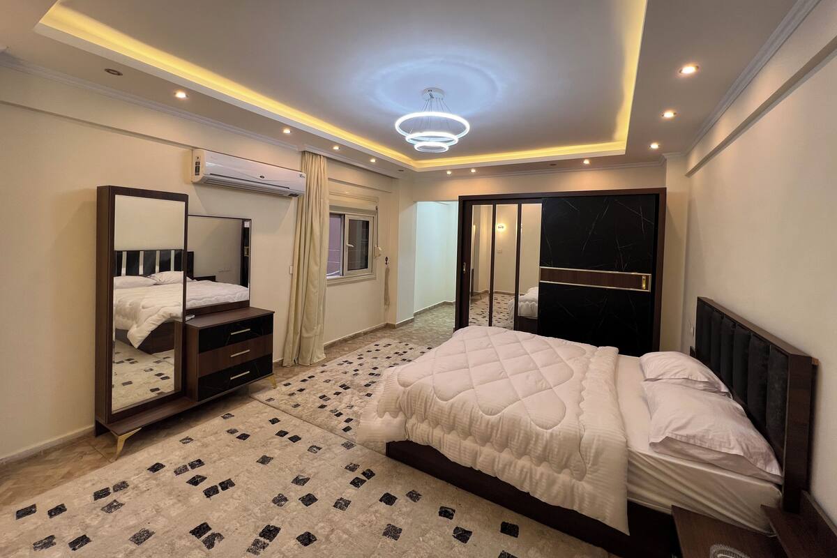 Quarto moderno com uma cama grande, guarda-roupa, espelho e luminária no teto.