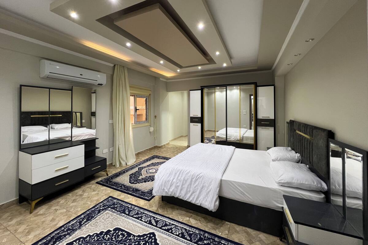 Quarto moderno com uma cama grande, guarda-roupa, espelho e luminária no teto.