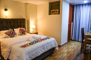 Quarto de hotel com cama, mesa de cabeceira, abajur, porta de madeira e uma cadeira.