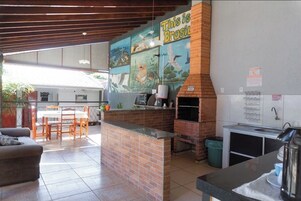 Uma cozinha com forno de tijolos, área de jantar com mesa e cadeiras, e um mural na parede.